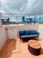 Terraço no telhado com um sofá azul, mesa de vime e cadeiras azuis.