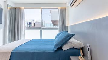 Quarto de hotel com cama, cortinas, janela e painel de controle fixado na parede.