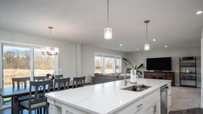 Uma cozinha espaçosa com uma ilha grande, luminárias pendentes modernas e vista para o exterior.