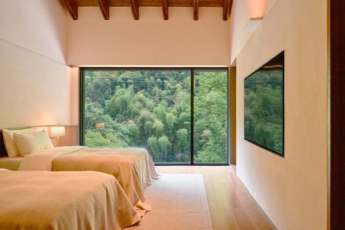 Quarto com duas camas, uma janela grande com vista para a floresta e um quadro na parede.