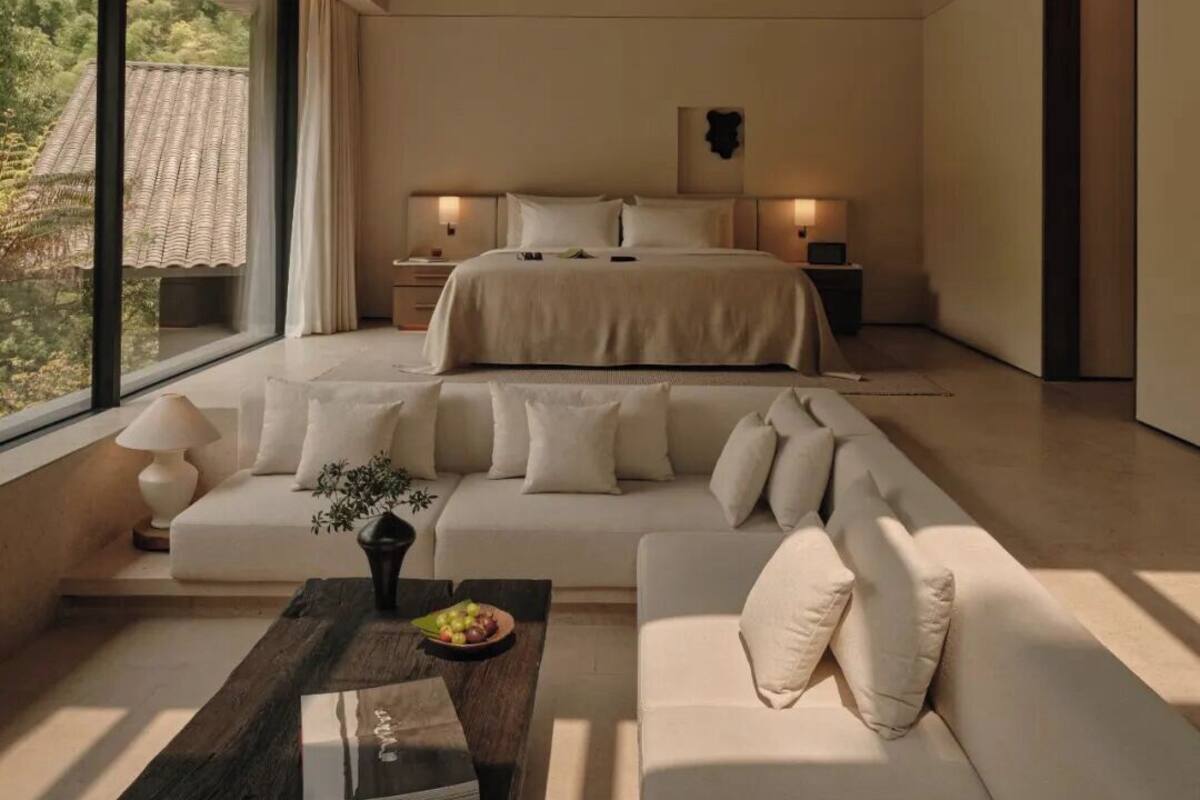 Quarto moderno com uma cama grande, um sofá, uma mesa de centro e vista para o verde lá fora.