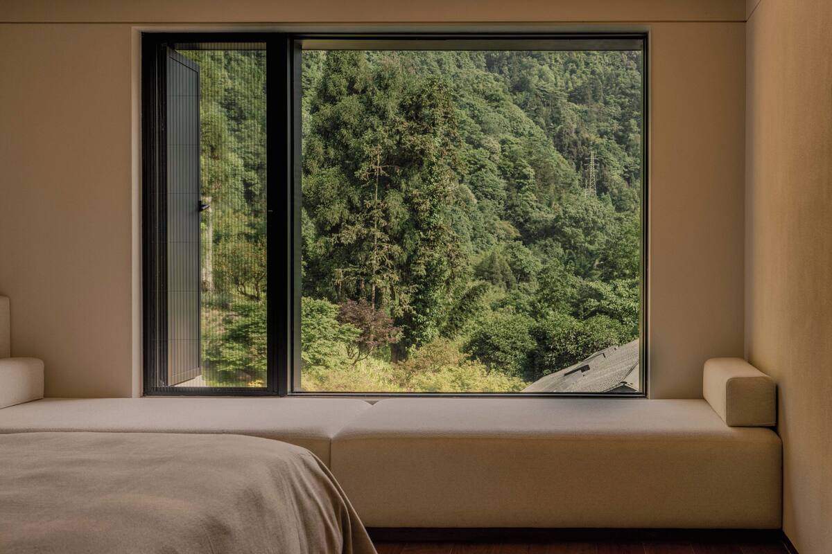 Quarto com uma janela grande, uma cama e vista para uma floresta.