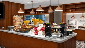 Uma área de buffet com diversos alimentos, um chef e uma cozinha moderna ao fundo.