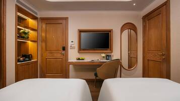 Quarto de hotel com duas camas, uma escrivaninha, uma cadeira, uma televisão e um espelho grande.