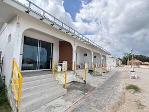 Um edifício com área externa coberta, escadaria com grades amarelas e céu claro.