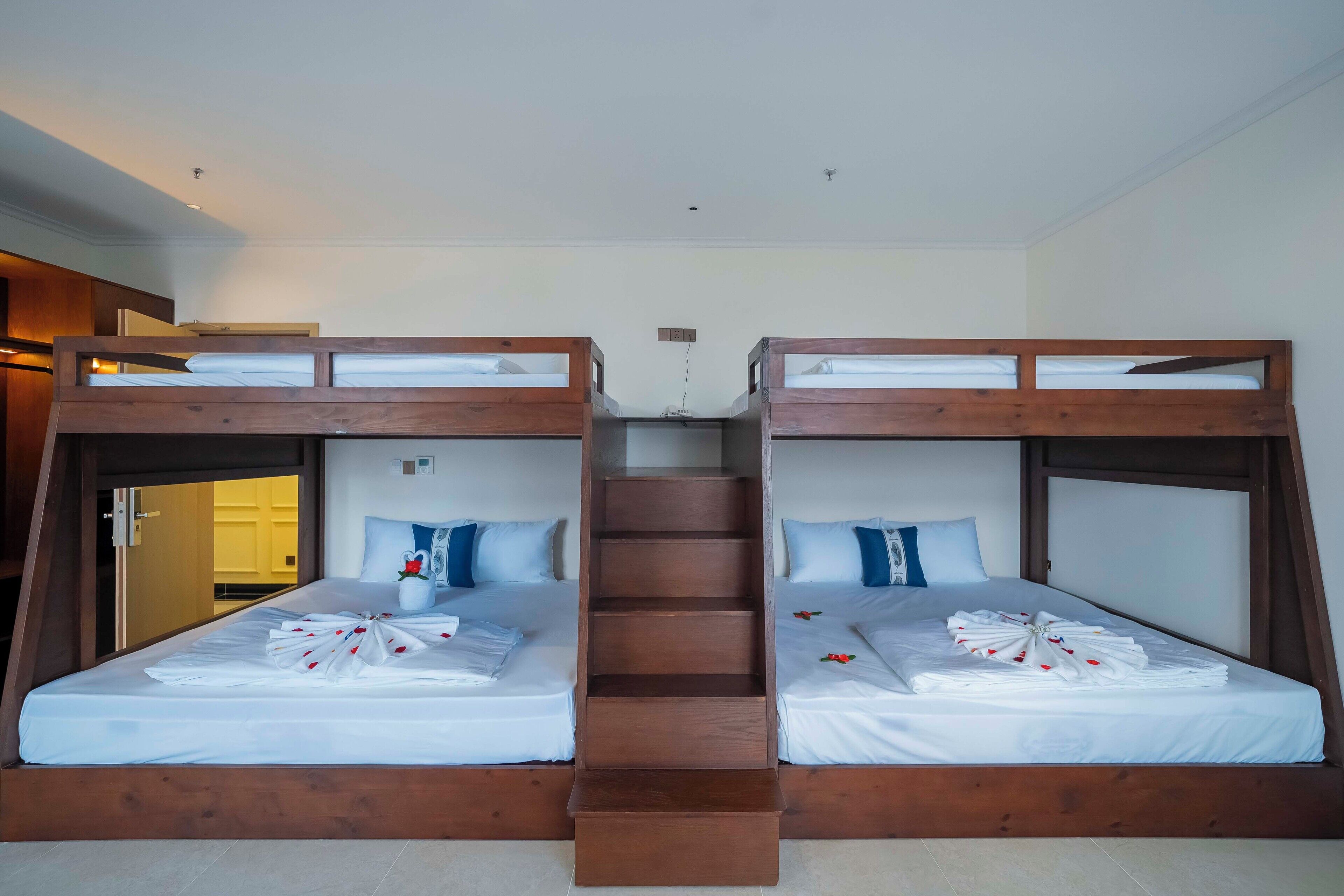 Quarto com duas beliches, escada de madeira e um pequeno banheiro visível através de uma porta aberta.