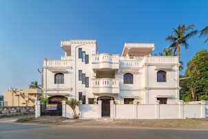 Um edifício branco de vários andares com varandas, entrada com portão e aviso de quartos disponíveis.
