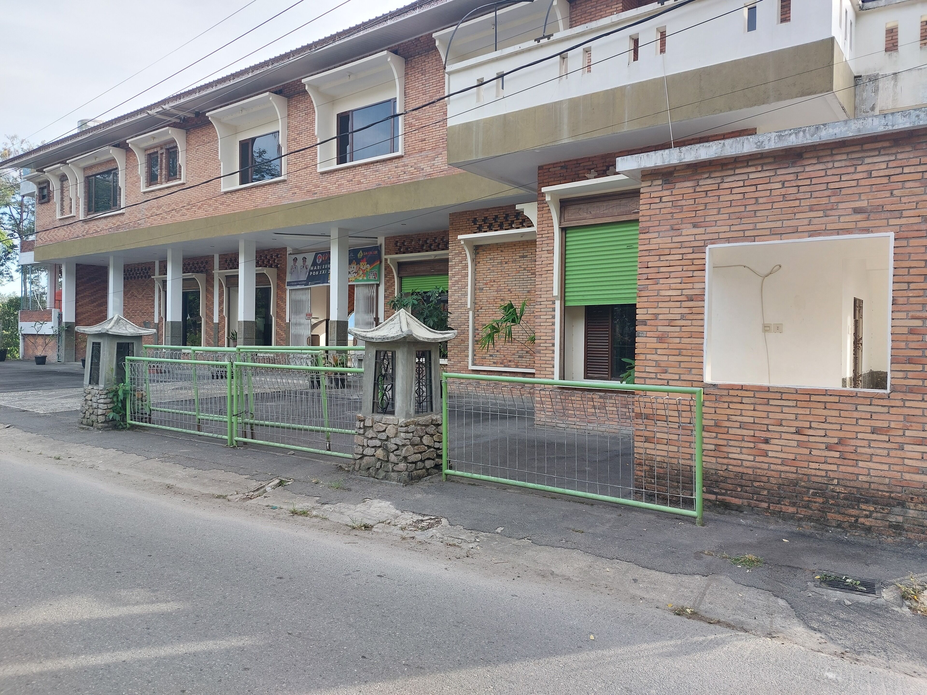 Um edifício de dois andares com fachada de tijolos, um portão verde e uma grande janela no andar térreo.