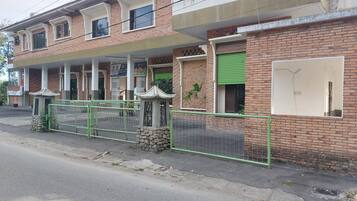 Um edifício de dois andares com fachada de tijolos, um portão verde e uma grande janela no andar térreo.