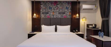 Quarto de hotel com uma cama grande, duas mesas de cabeceira, um criado-mudo, aparelho de ar condicionado, abajur e uma tapeçaria decorativa na parede.