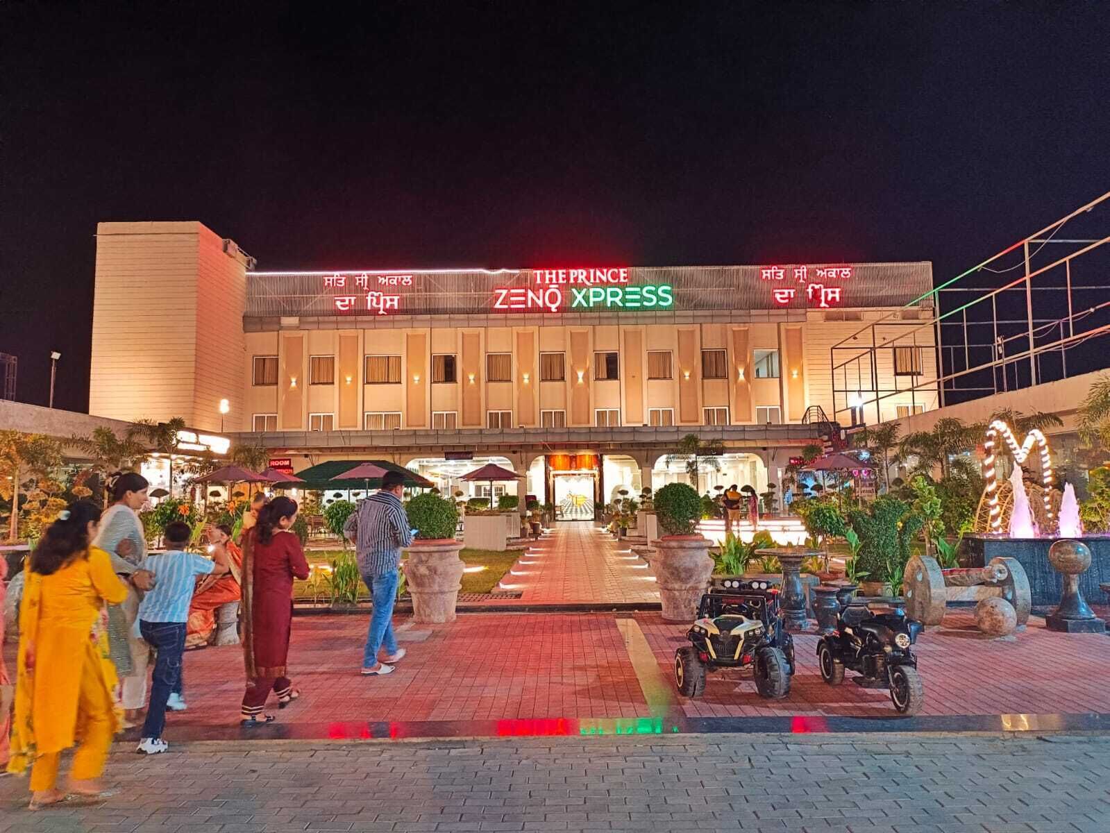 Um hotel chamado 'The Prince Zenith Xpress', com fachada moderna, entrada coberta e um pátio ajardinado com detalhes decorativos.