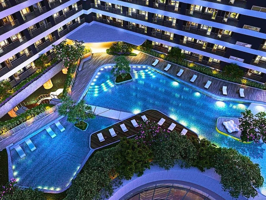 Um hotel com vários andares, uma grande piscina iluminada rodeada por vegetação exuberante e áreas de estar ao ar livre.