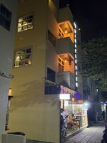 Um edifício de vários andares com janelas iluminadas e uma loja bem iluminada no andar térreo.