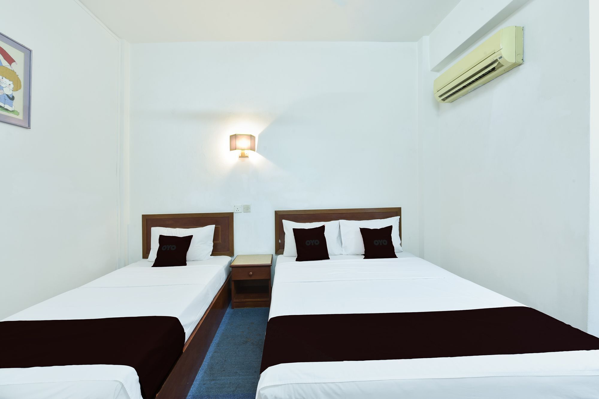 Quarto de hotel com duas camas de solteiro, uma mesinha de cabeceira, ar condicionado fixado na parede e luminária na parede.