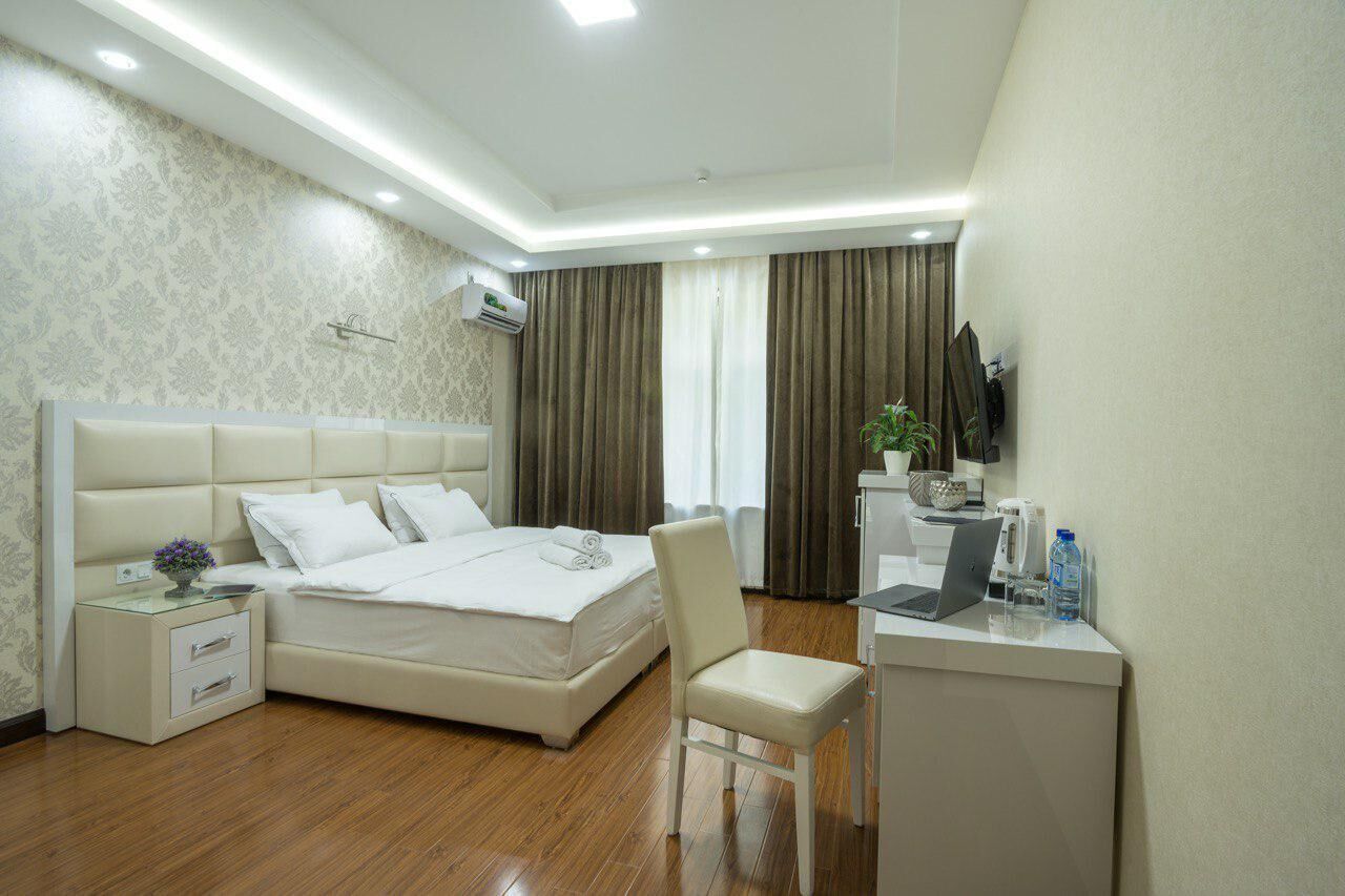 Quarto de hotel com cama, mesa de cabeceira, cadeira, escrivaninha e televisão.