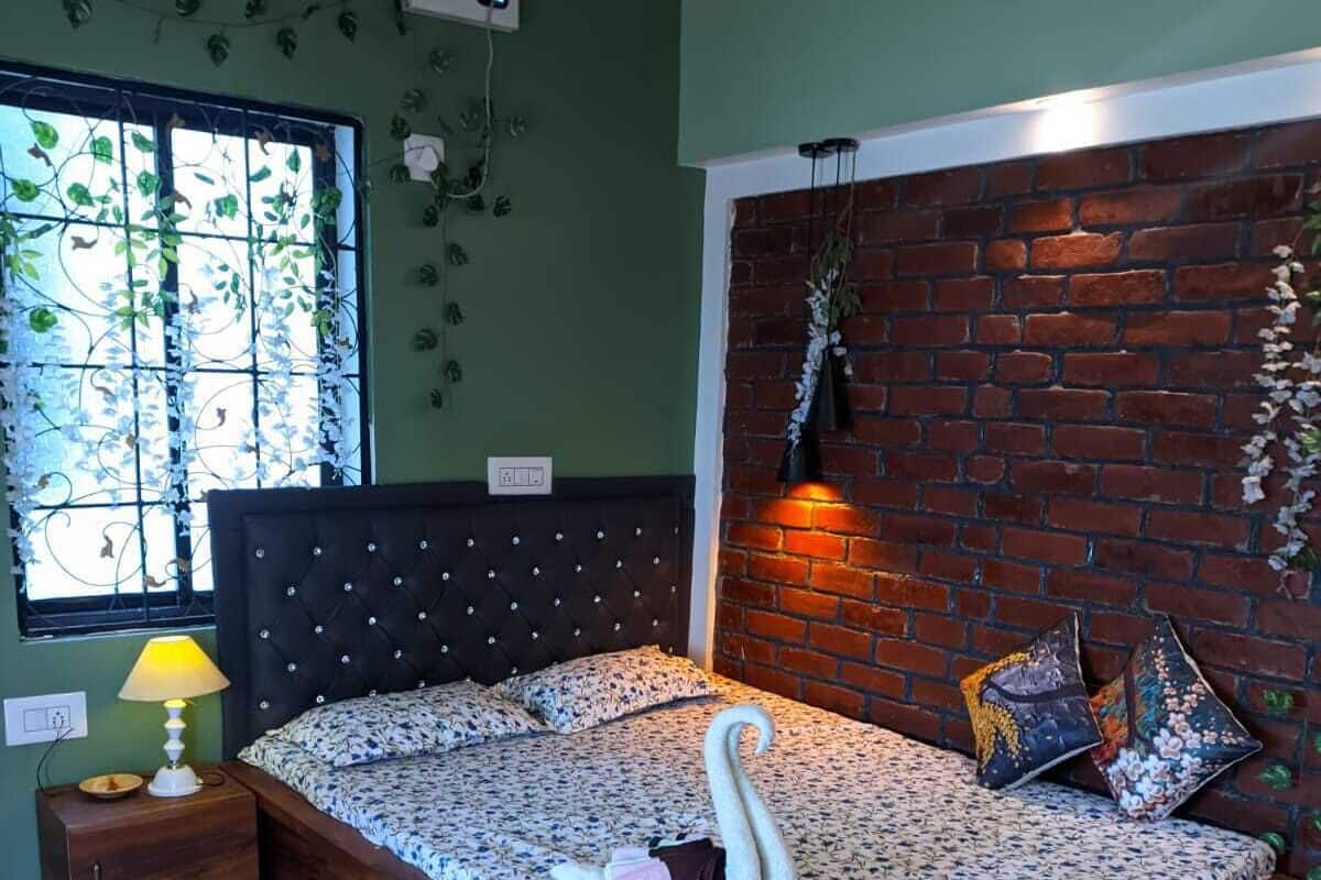 Quarto com cama adornada com desenho de cisne, parede de tijolos decorativa, janela com vegetação e mesa de cabeceira com abajur.