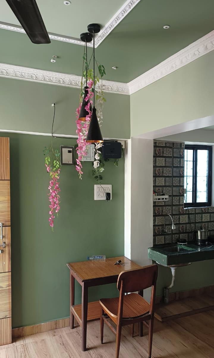 Uma área de refeições com mesa e cadeiras de madeira, um arranjo floral pendente e uma cozinha ao fundo.