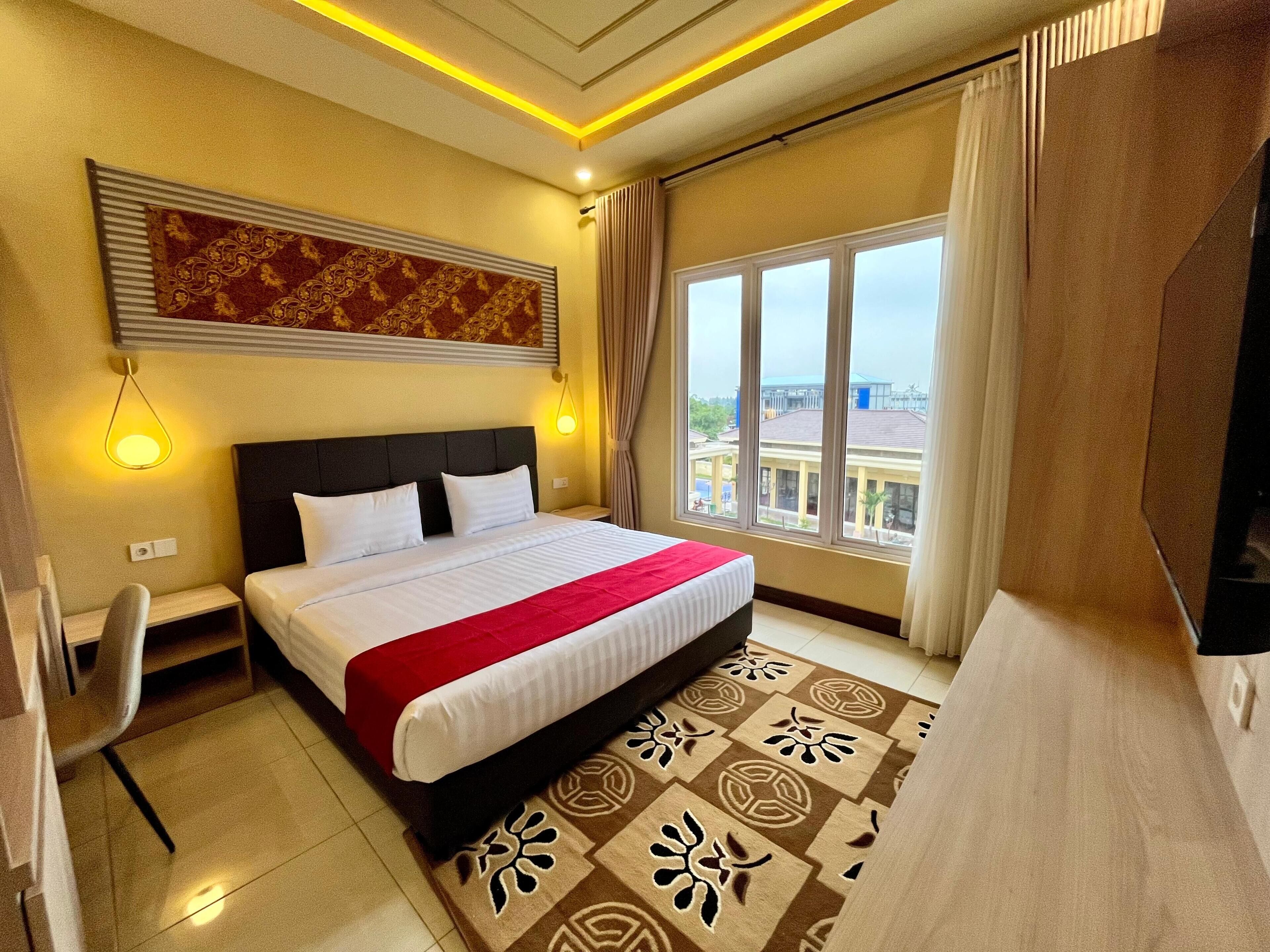 Quarto de hotel com uma cama grande, uma escrivaninha, uma cadeira, janela com vista e um objeto decorativo na parede.