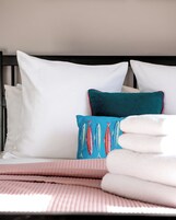 Cama bem arrumada com almofadas brancas e azul-esverdeadas, um cobertor rosa e uma cabeceira preta.