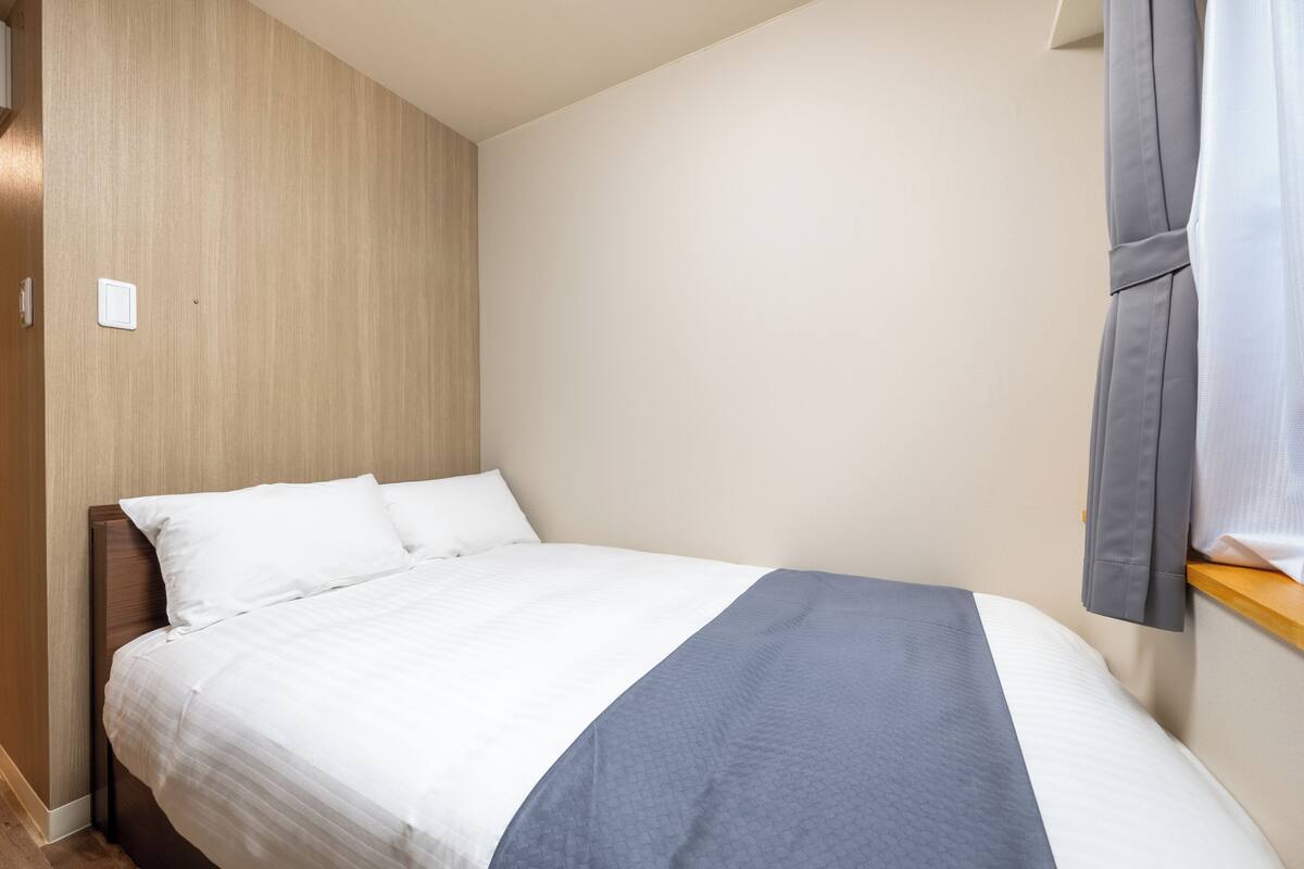 Cama bem arrumada com roupa de cama branca e azul, cabeceira de madeira e parede em tom claro.