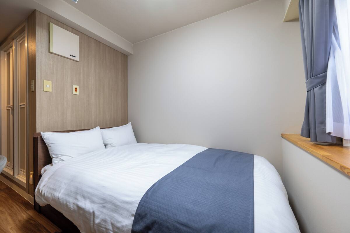 Quarto de hotel com uma cama, guarda-roupa de madeira e uma pequena mesa de madeira com cortina.
