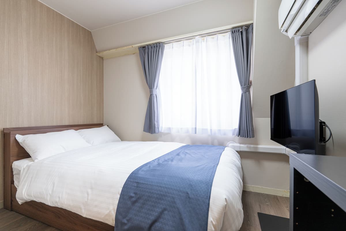 Quarto de hotel com cama, televisão de tela plana e janela com cortinas.