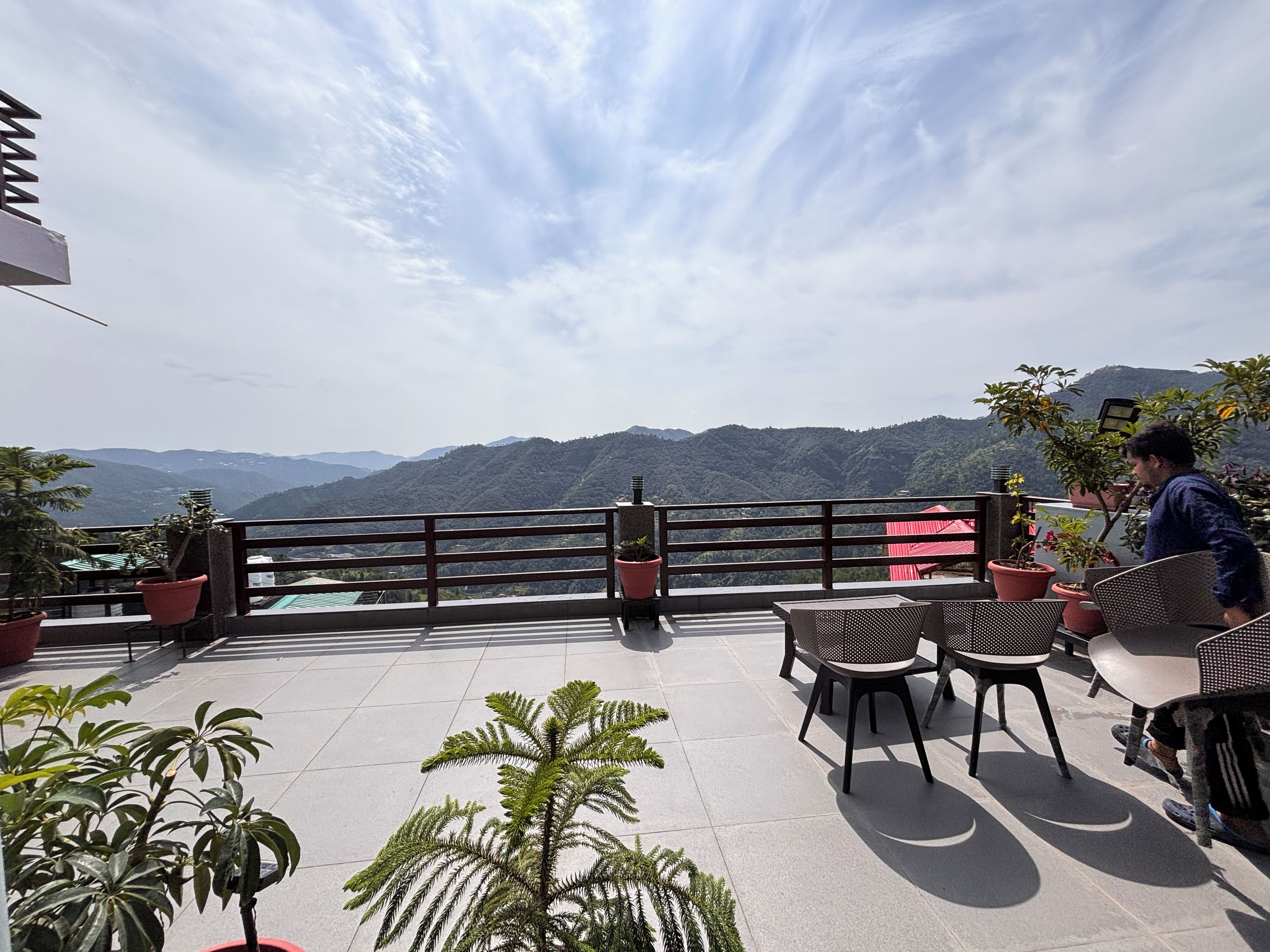 Terraço com plantas em vasos, área de estar externa e vista para montanhas ao longe.