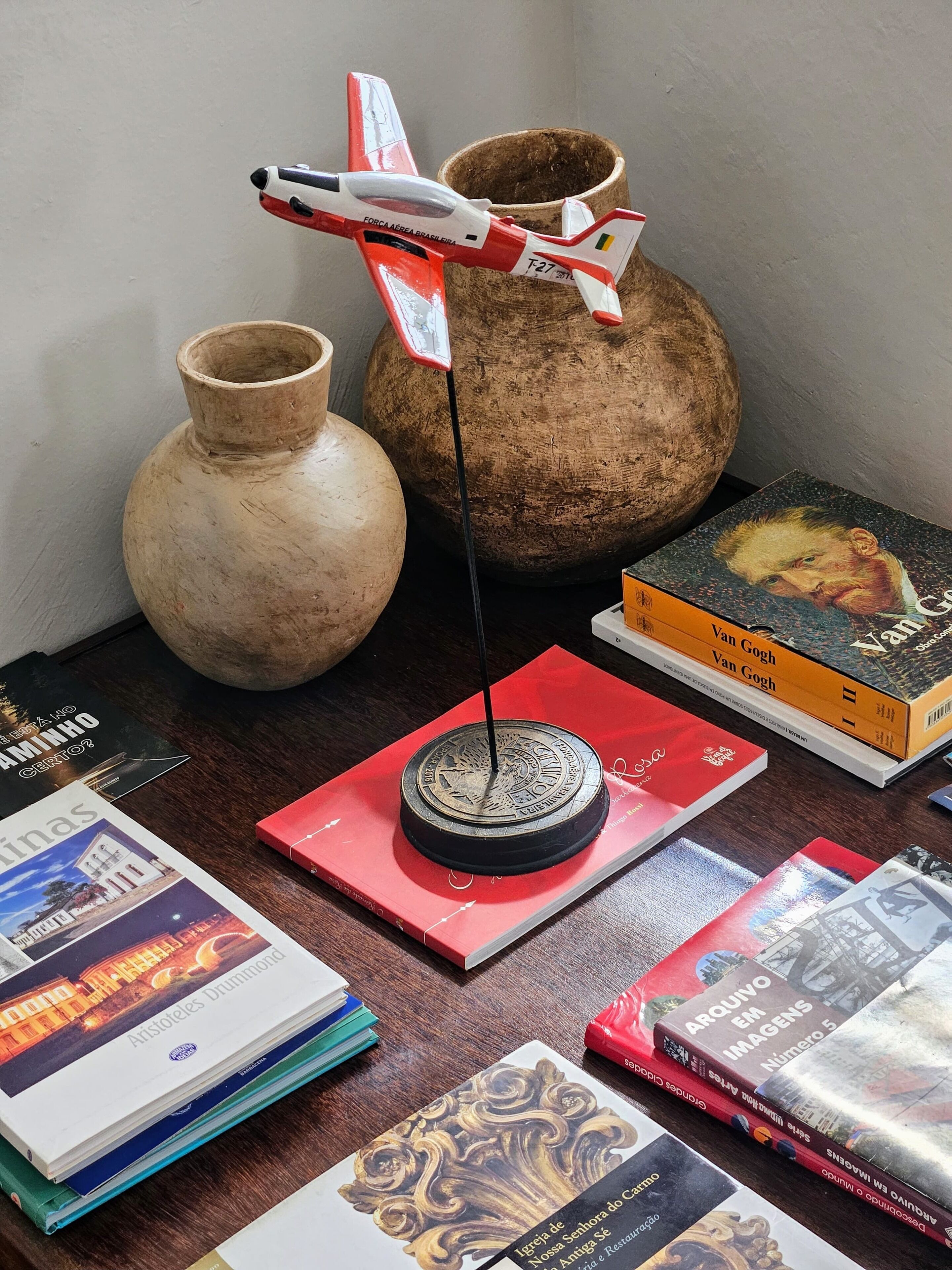 Uma mesa de madeira com livros, uma bússola decorativa e um modelo de avião.