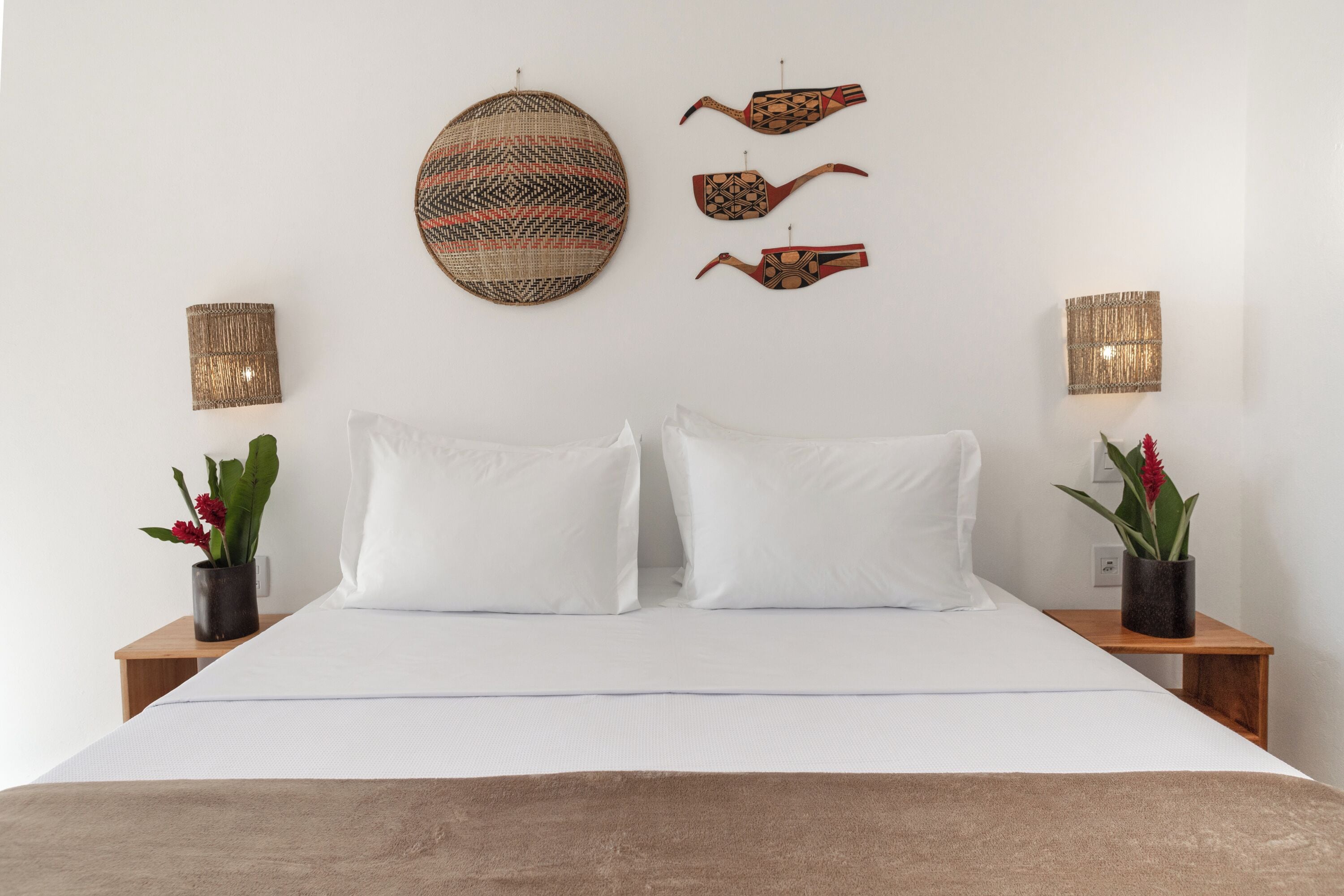 Uma cama bem arrumada com lençóis brancos, duas mesas de cabeceira com abajures e detalhes decorativos nas paredes.