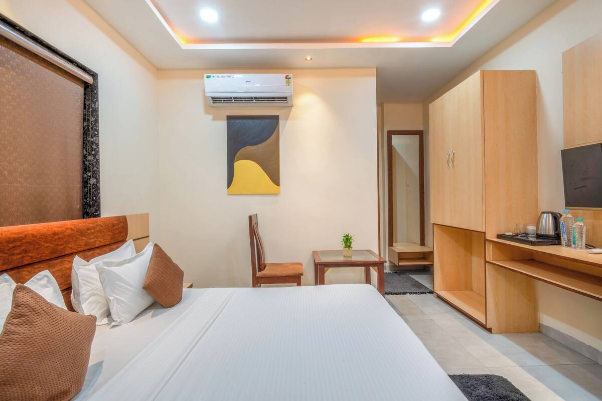 Quarto de hotel com cama, escrivaninha, cadeira, ar condicionado e um quadro na parede.