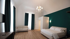 Quarto de hotel moderno com piso de madeira, uma cama branca, um sofá branco, uma escrivaninha e uma TV.