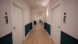 Corredor de hotel com portas brancas, detalhes em verde-água e piso de madeira.