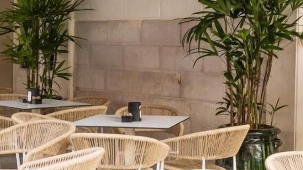 Uma área de estar ao ar livre com cadeiras e mesas de vime, um letreiro com a inscrição 'EXTRA BAR-BISTROT' e plantas em vasos.