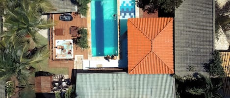 Vista aérea de uma propriedade com piscina retangular, área de varanda coberta e estrutura de telhado laranja.