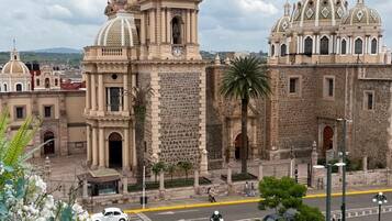 Uma catedral histórica com duas torres sineiras e uma cúpula grande, rodeada por uma praça com bancos e uma rua.