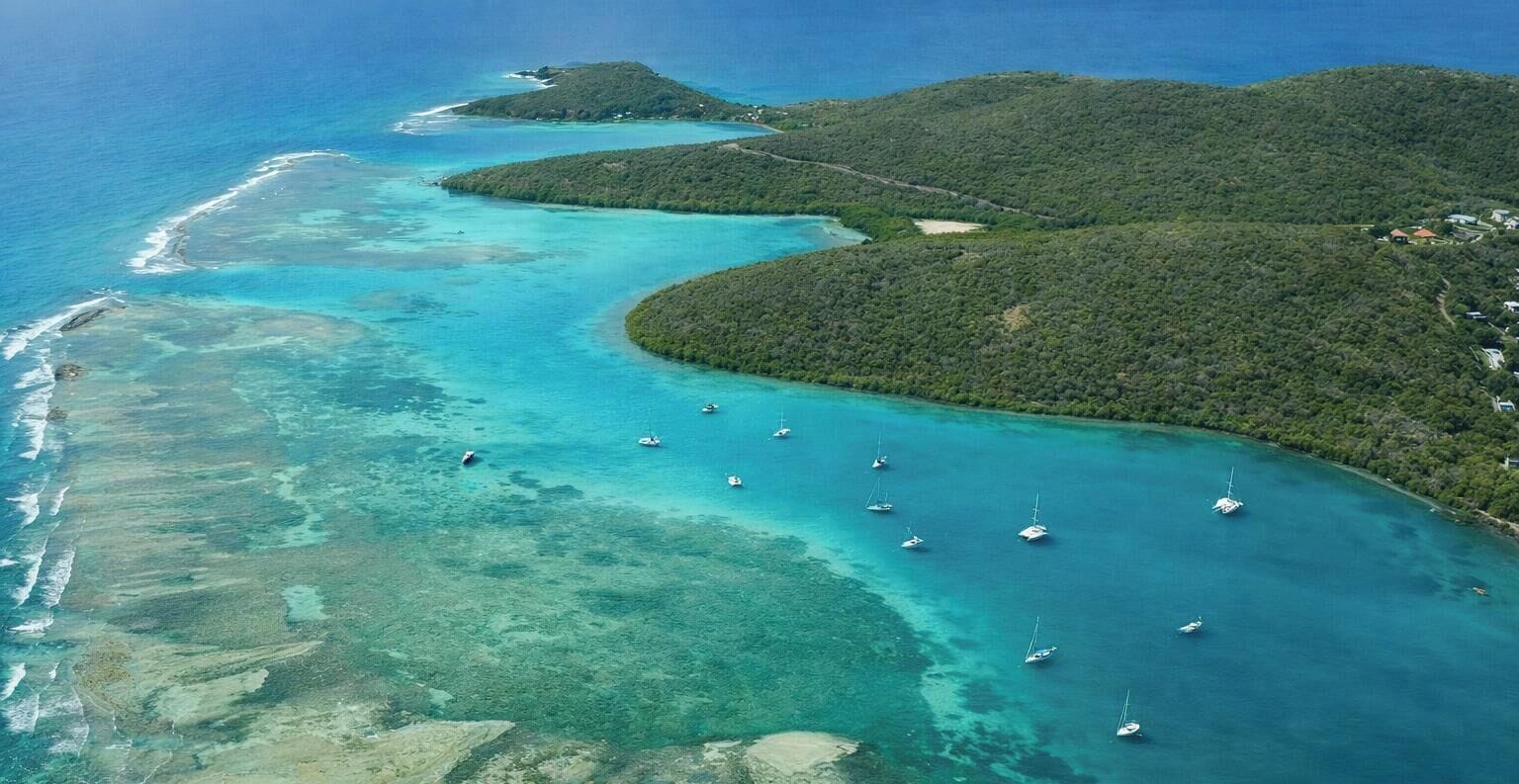 Vista aérea de uma área costeira com águas turquesa cristalinas, algumas ilhas pequenas e muitos barcos ancorados na baía.
