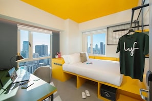Quarto de hotel moderno com uma cama, uma escrivaninha com um laptop e uma janela vista para a cidade.