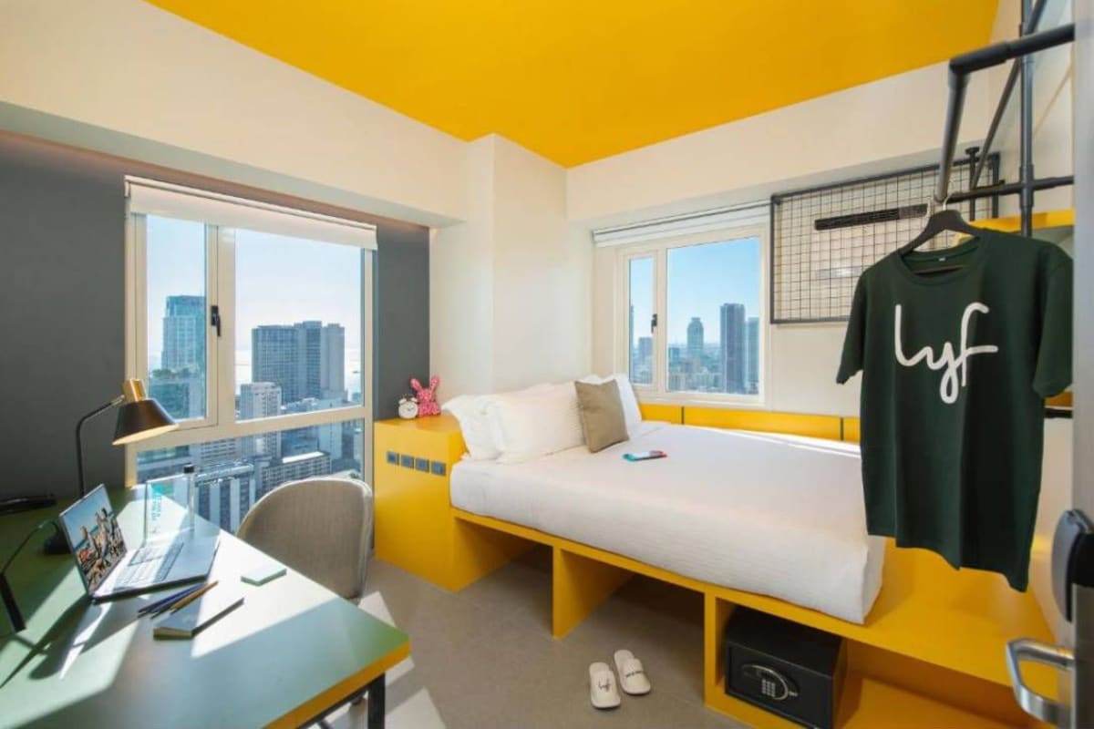 Quarto moderno com cama, escrivaninha e janela com vista para a cidade.