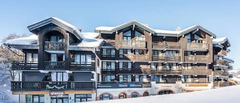 Um edifício alto para aluguer de esqui com varandas e grandes janelas, rodeado por neve.