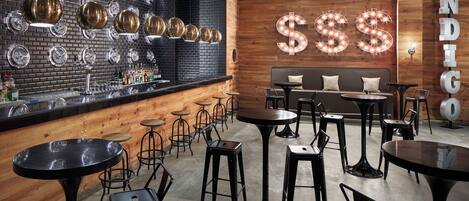Uma área de bar moderna com parede de tijolos, mesas redondas e banquetas.