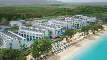 Um resort com vários edifícios, piscina e praia com guarda-sóis.