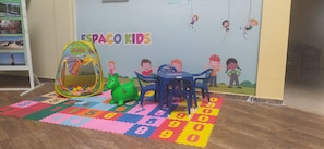 Espaço de brincadeiras infantis com um tapete colorido, piscina de bolinhas e um brinquedo de dinossauro.