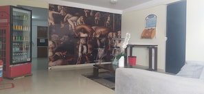 Uma sala de estar com uma máquina de vendas vermelha, um sofá branco, um mural e uma pequena mesa com uma planta em vaso.