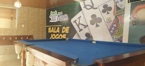 Uma mesa de bilhar em um ambiente com parede revestida de azulejos e um cartaz anunciando Hotel Aracaju Express.