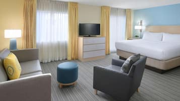 Quarto de hotel com uma cama, duas poltronas, um sofá, uma televisão sobre um móvel e um abajur.