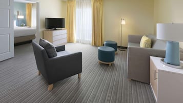 Quarto de hotel com cama, dois sofás, televisão, abajur e luminária de chão.
