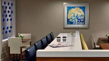 Uma área de refeições de hotel com uma mesa comprida, cadeiras de couro e um quadro na parede.