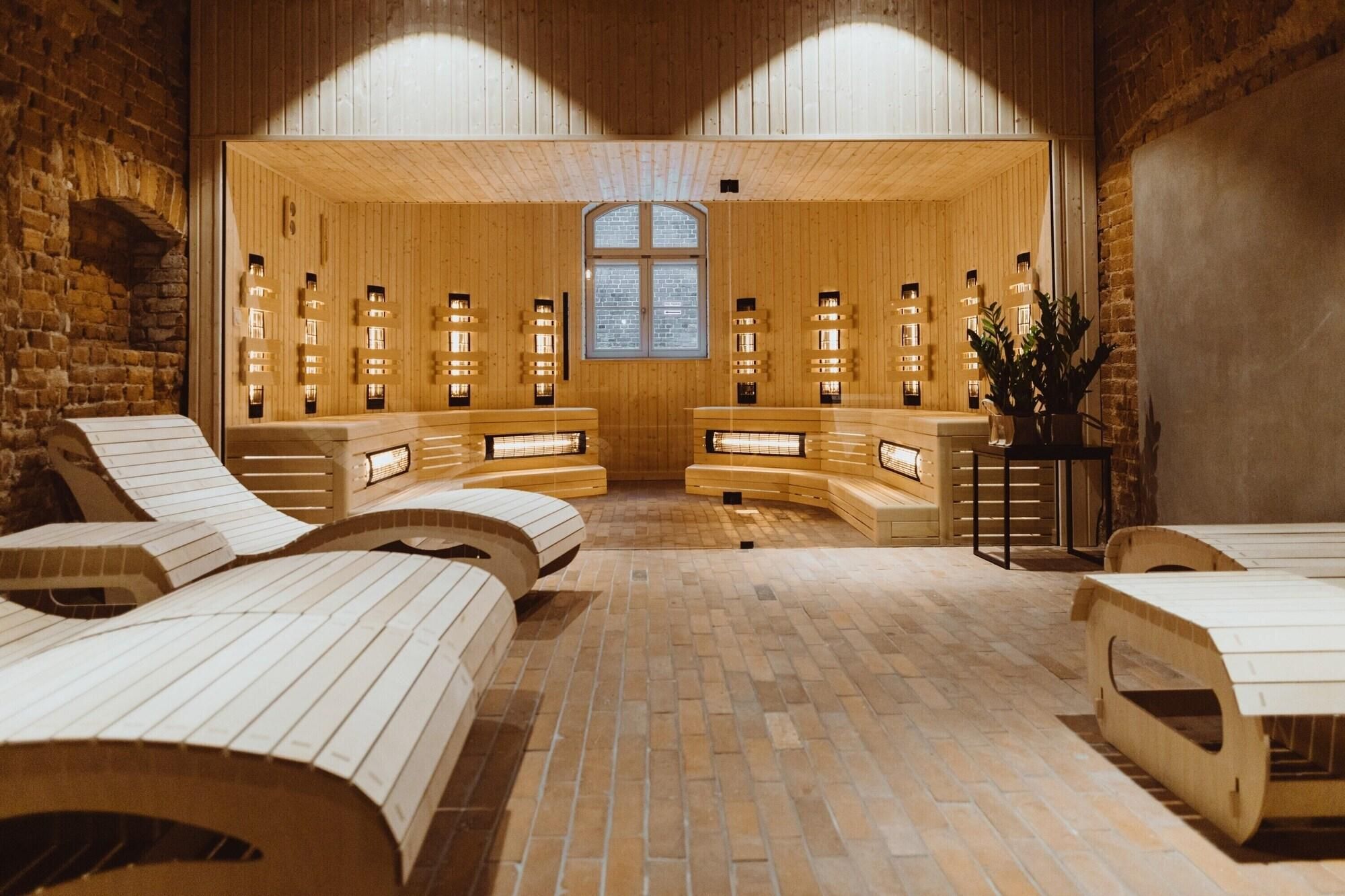 Sala de sauna com bancos e assentos de madeira, parede de tijolos e janela.