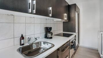 Uma cozinha moderna com armários escuros, uma pia de aço inoxidável, uma cafeteira e um forno embutido.