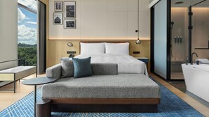 Quarto de hotel moderno com uma cama grande, uma mesa pequena, um sofá, banheiro com banheira e vista para a cidade.